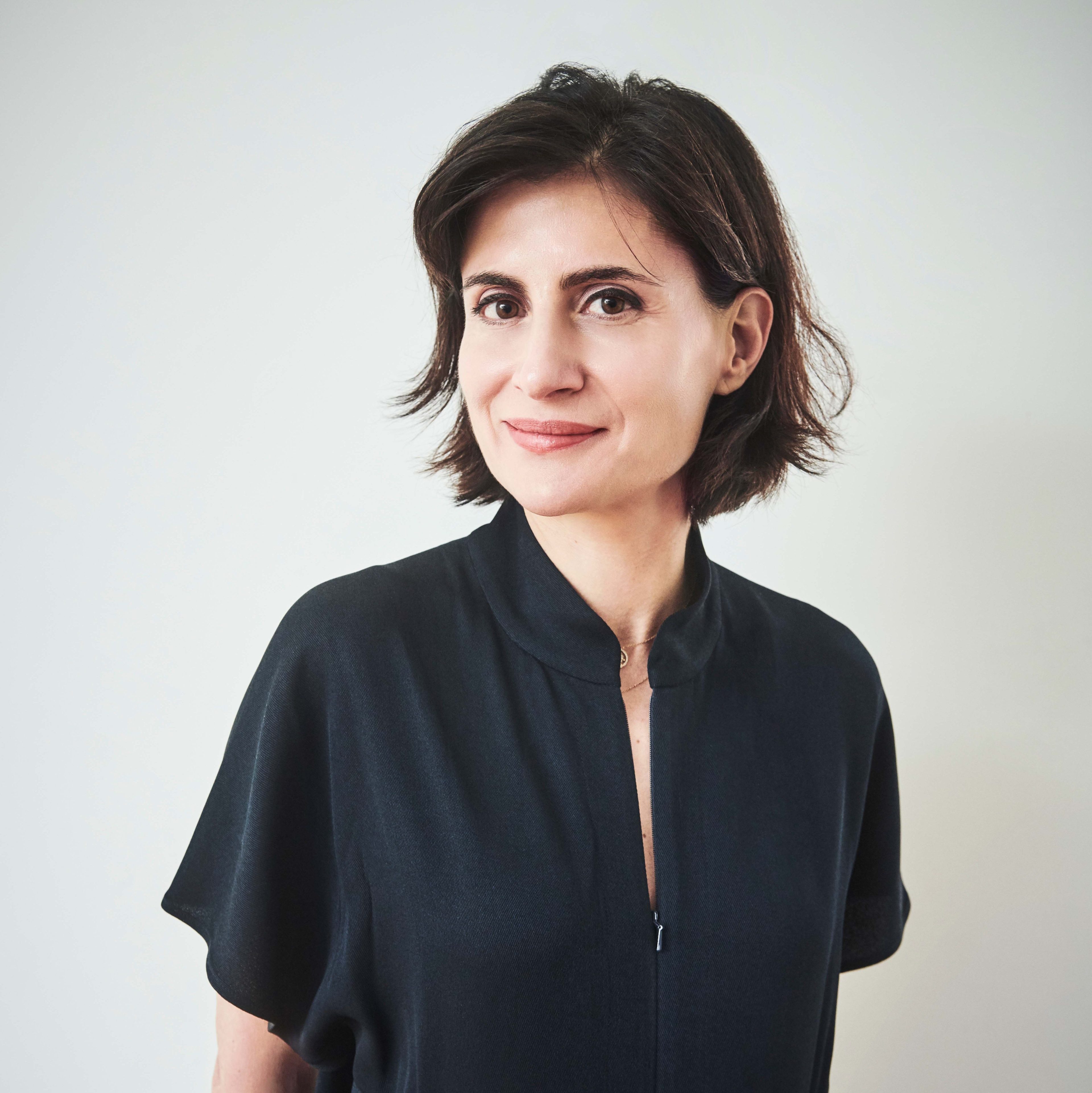 person with neck length brown hair standing against wall