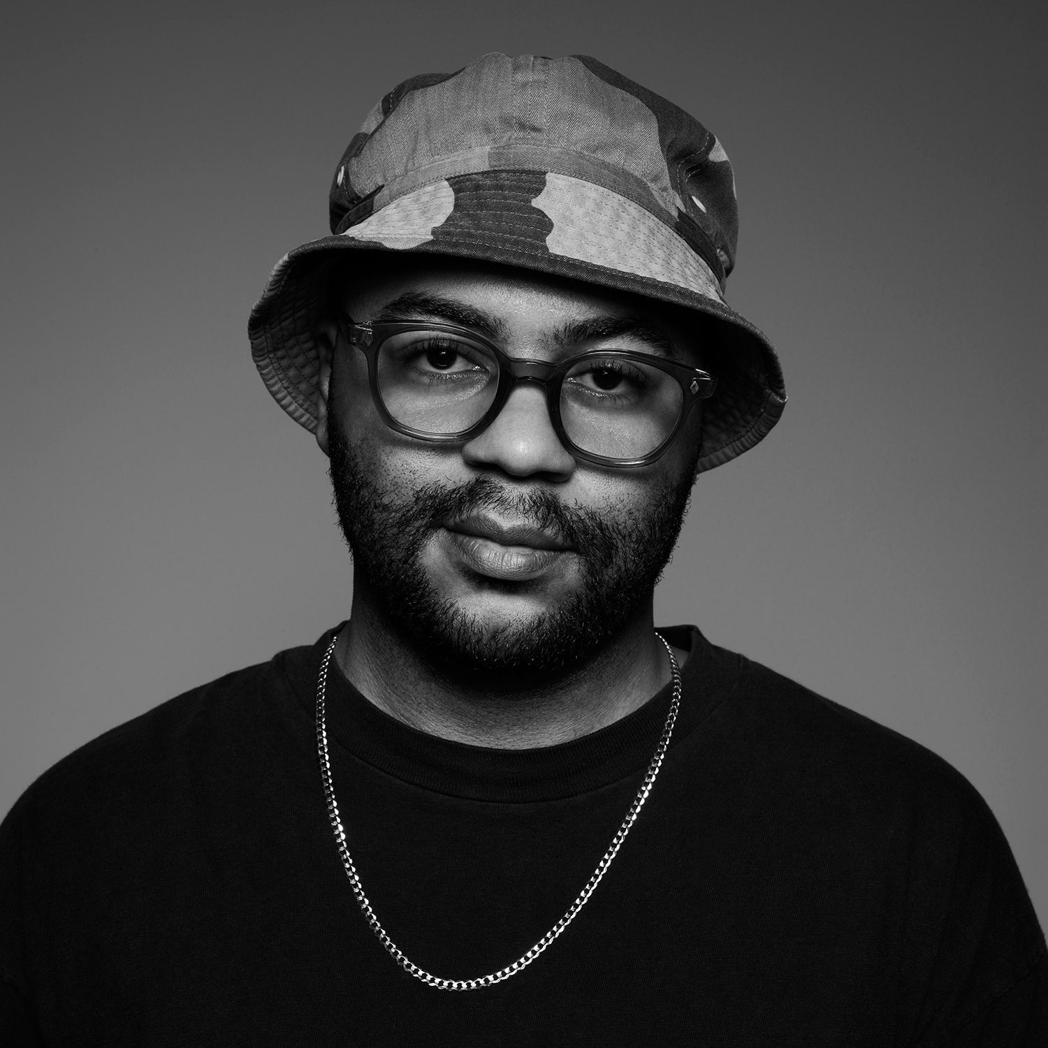 black and white image of a person with a bucket hat and glasses smirking