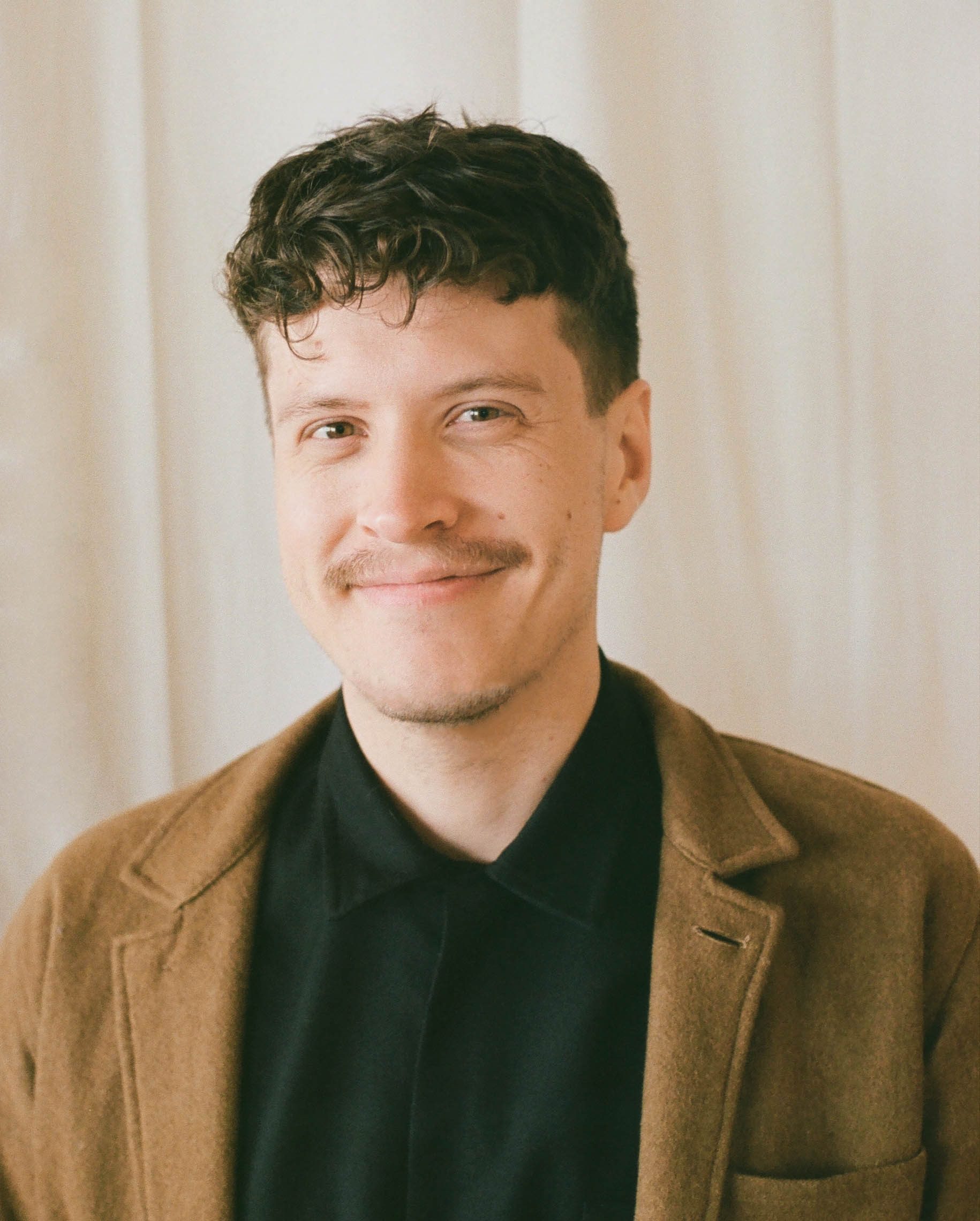 daniel headshot in a black tee and tan blazer